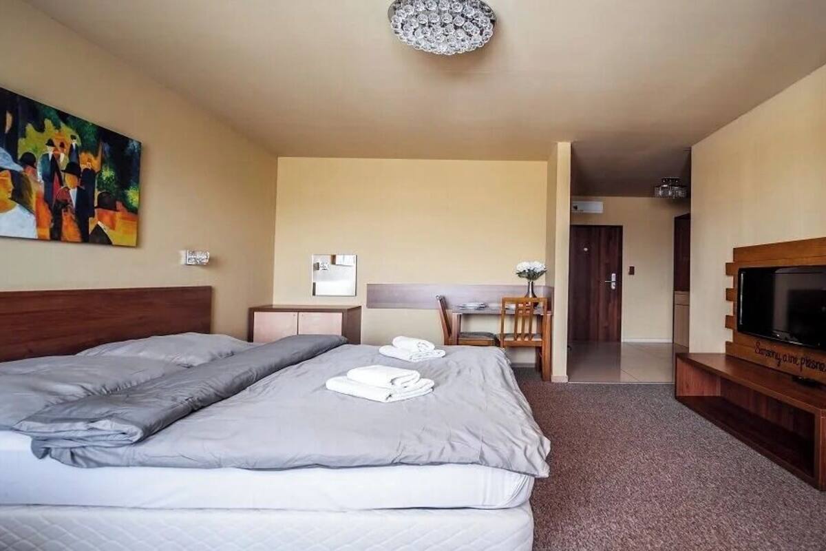 Quarto de hotel com cama, escrivaninha, televisão e um quadro na parede.