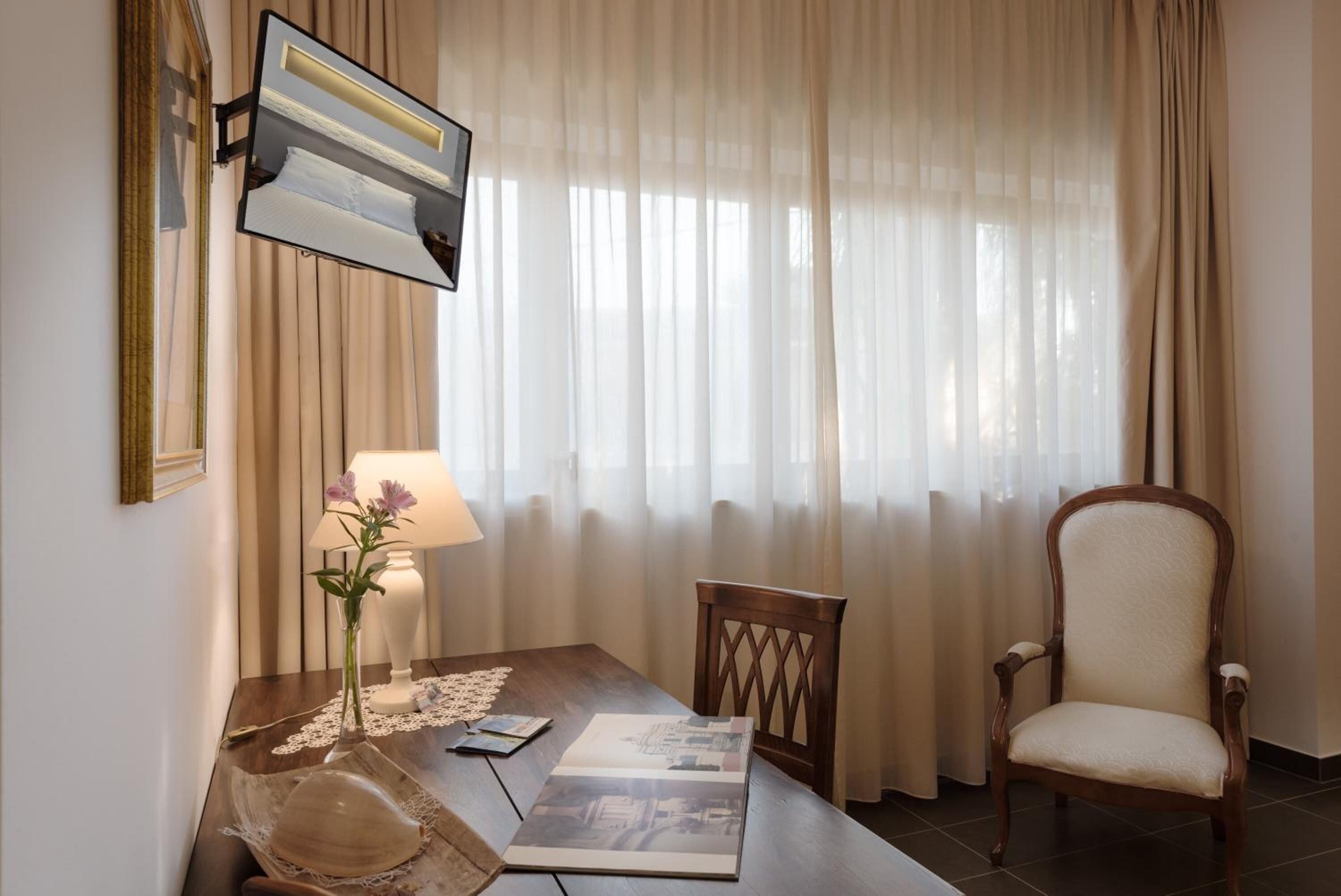 Quarto de hotel com uma escrivaninha de madeira, uma cadeira, um abajur, um porta-retrato e uma TV fixada na parede.