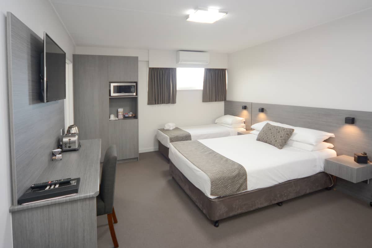 Quarto de hotel com duas camas, uma escrivaninha com computador e cafeteira, televisão e janela com cortinas.