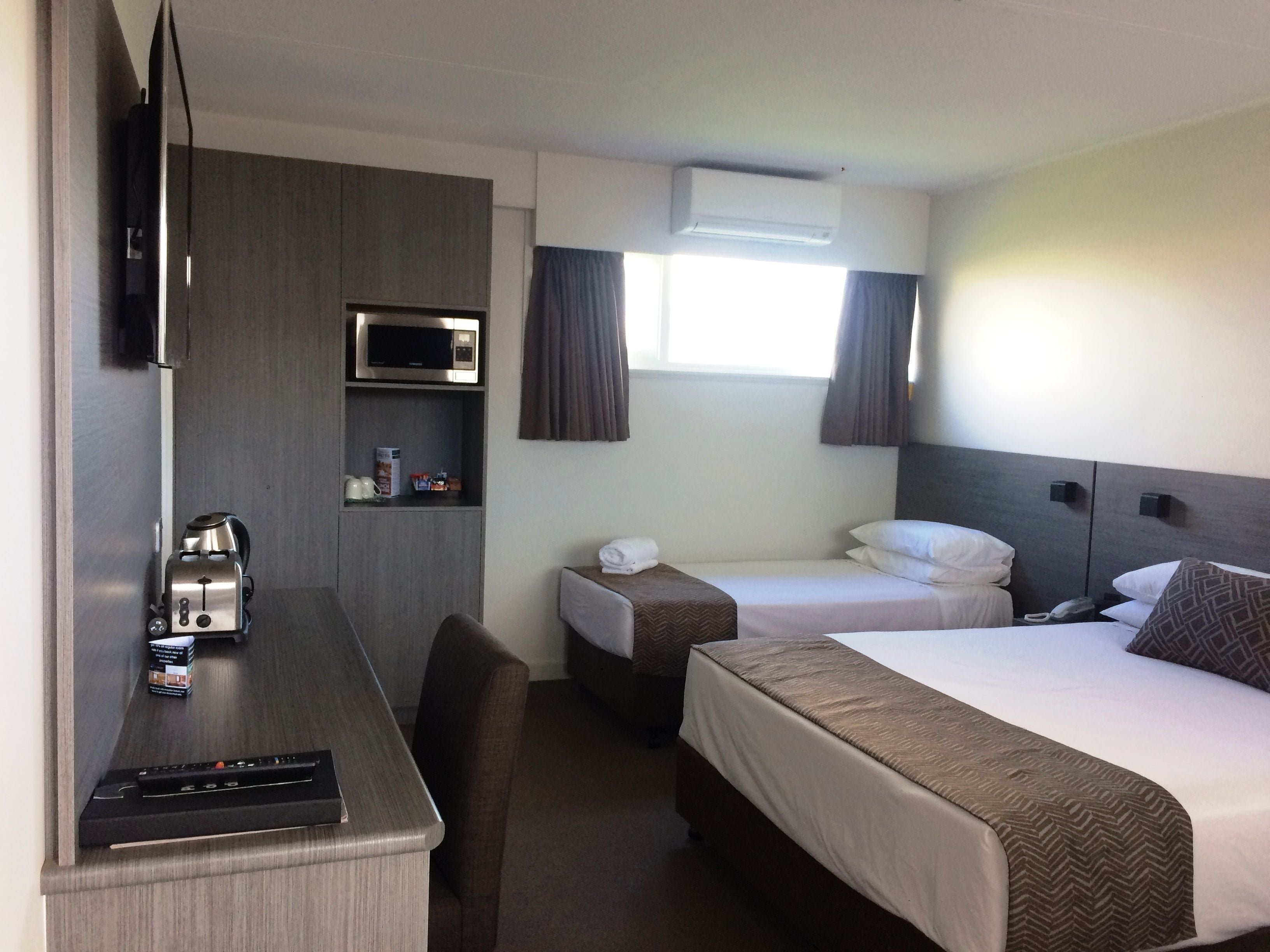 Quarto de hotel com cama, escrivaninha com micro-ondas, televisão e um pequeno espaço de estar.