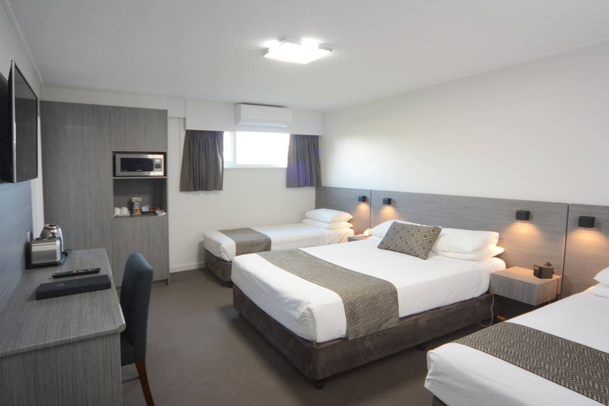 Quarto de hotel com duas camas de solteiro, uma mesa com micro-ondas, televisão e uma cadeira.