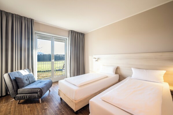 Quarto de hotel com duas camas, um sofá e uma janela grande com cortinas.