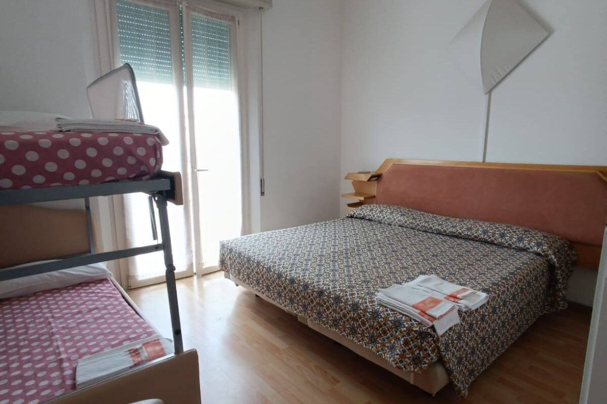 Quarto com beliche, uma cama de solteiro e janela com persianas.