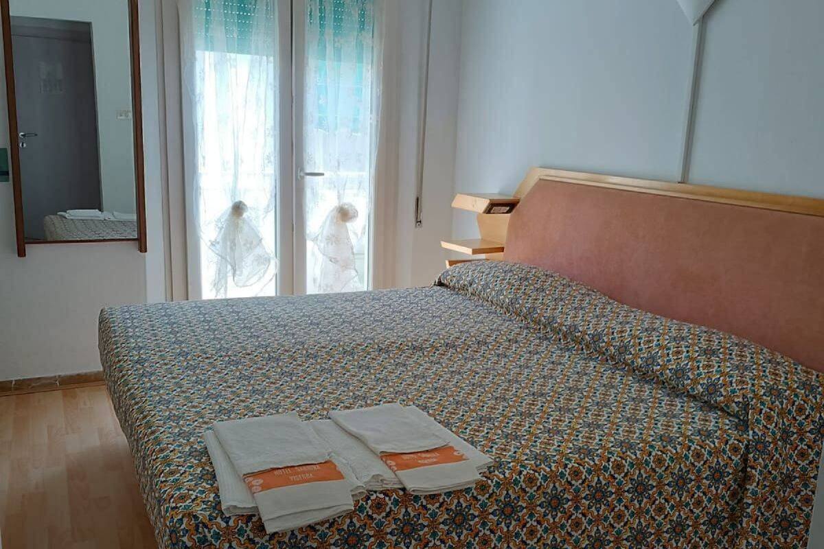 Quarto com cama, espelho, janela com cortinas e mesa de cabeceira.