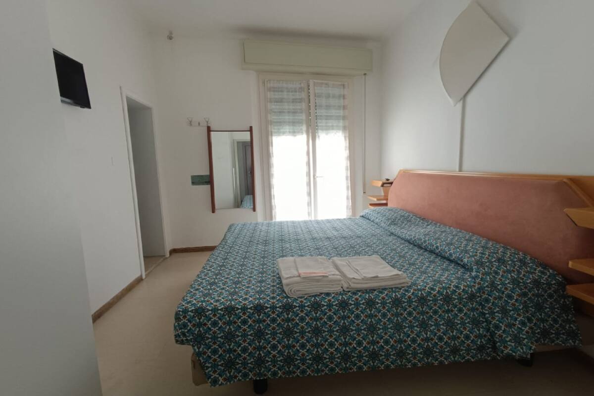 Quarto com cama, cabeceira de madeira, espelho e janela com cortinas.