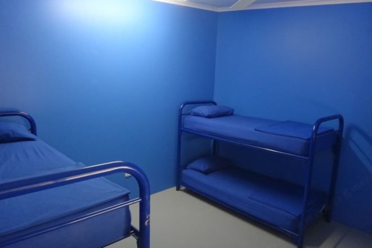 Quarto com duas beliches, uma à esquerda e outra à direita, ambas com estrutura de metal e roupa de cama azul.