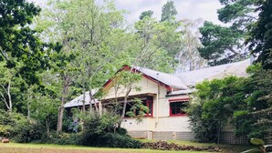 Uma casa com telhado vermelho e paredes brancas, cercada por árvores e uma cerca.
