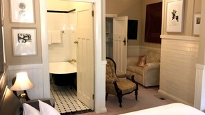 Quarto com cama, uma cadeira, uma luminária e banheiro visível por uma porta aberta.
