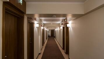 Um corredor de hotel com portas de madeira, chão coberto de carpete e luminárias fixadas na parede.