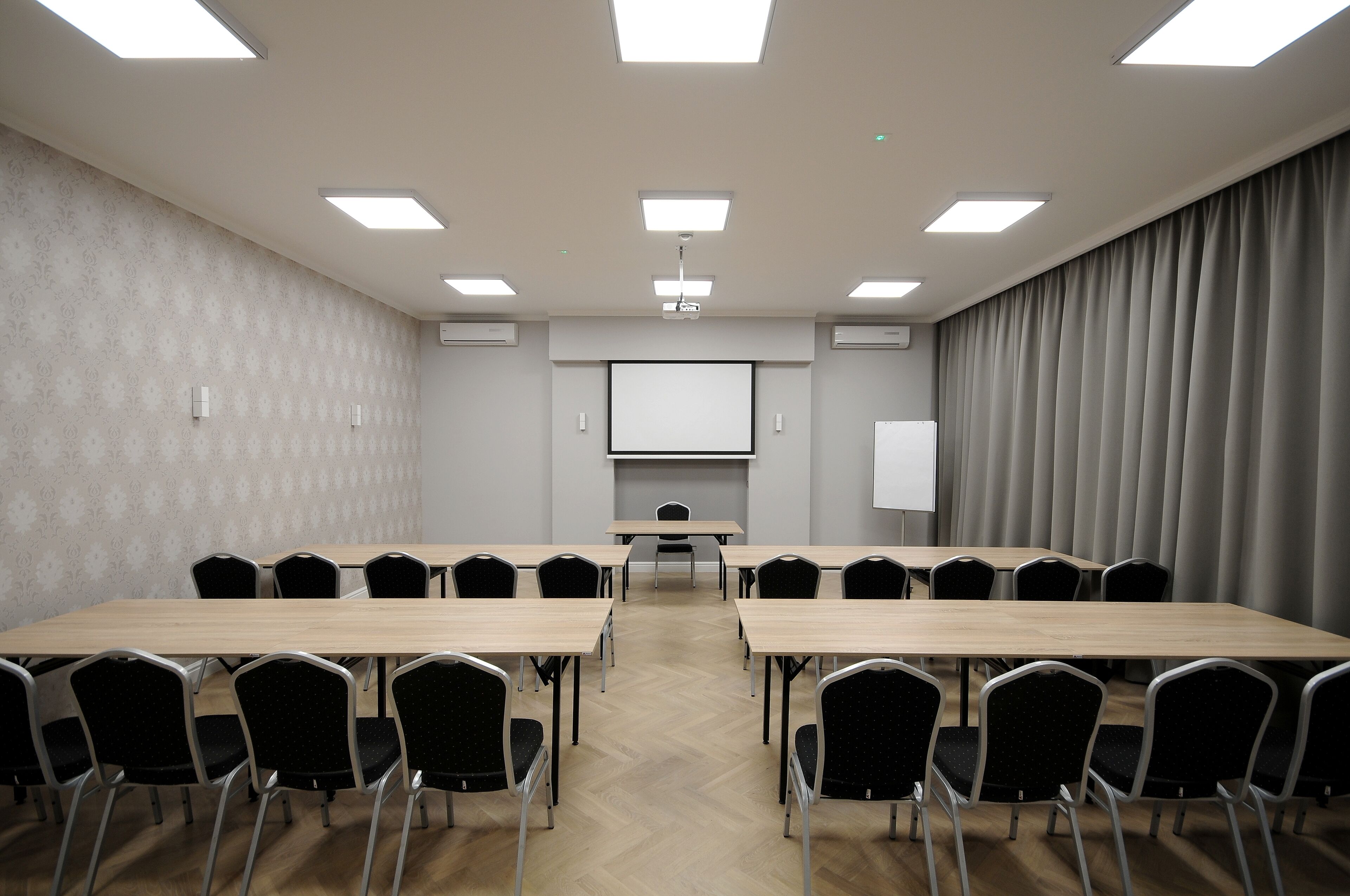 Uma sala de conferências com uma mesa grande, cadeiras, uma tela de projetor e um quadro branco.