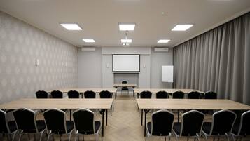 Uma sala de conferências com uma mesa grande, cadeiras, uma tela de projetor e um quadro branco.
