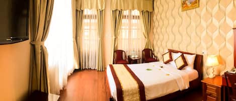 Quarto de hotel com cama, mesa de cabeceira, abajur, espelho e televisão fixada na parede.