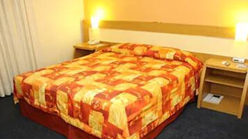Quarto de hotel com uma cama grande, uma mesinha de cabeceira, uma luminária e um telefone.