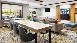 Um lobby de hotel moderno com uma grande mesa de madeira, assentos confortáveis e uma ampla janela com vista para o exterior.