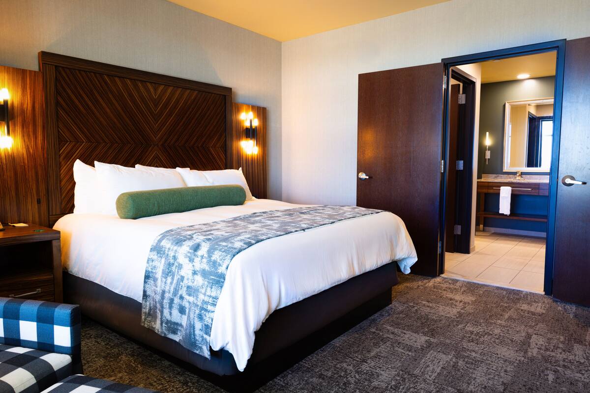 Uma cama bem arrumada com cabeceira de madeira, mesa de cabeceira e criadeira.