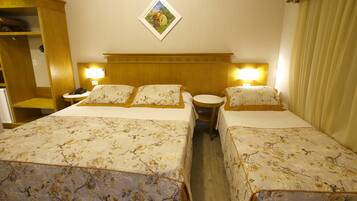 Quarto de hotel com duas camas, uma cabeceira de madeira, uma mesinha de cabeceira com telefone e um quadro na parede.