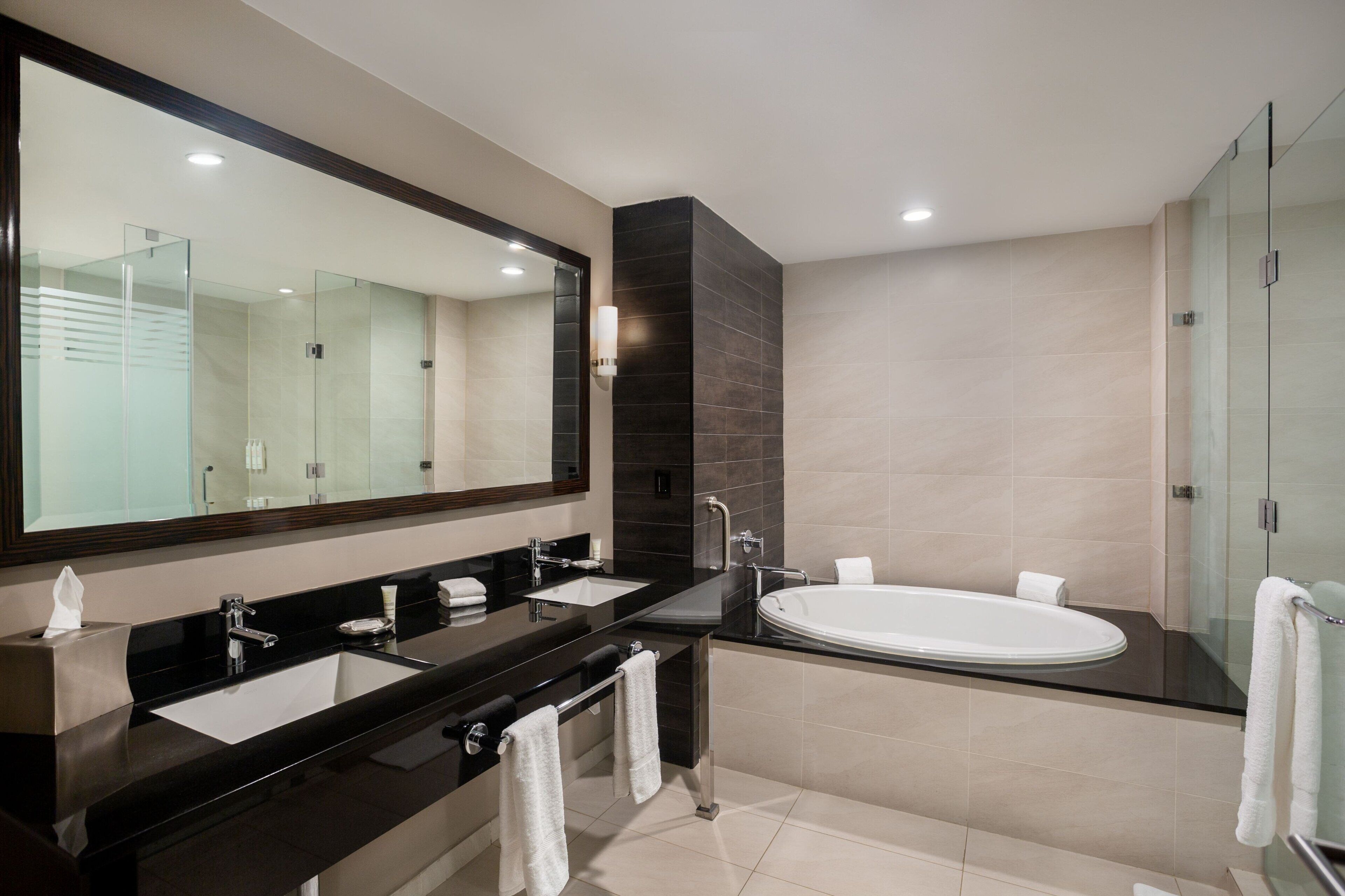 Uma casa de banho moderna com duas pias, um espelho grande, uma banheira e um chuveiro com divisória de vidro.