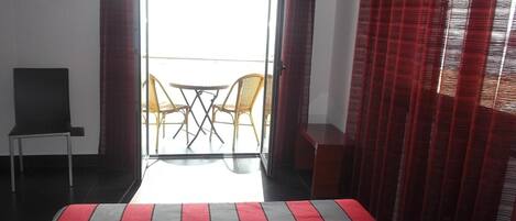 Quarto de hotel com cama, uma cadeira, mesa pequena e varanda com cadeiras.
