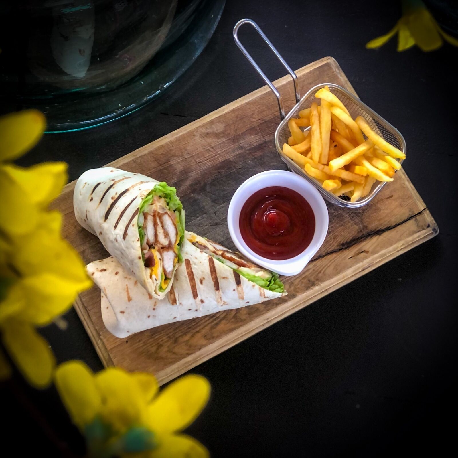 Um wrap com batatas fritas e ketchup sobre uma tábua de madeira.