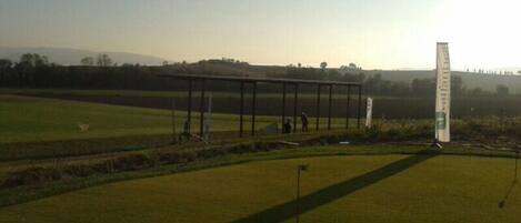 Campo de golfe com driving range coberto e haste de bandeira em primeiro plano.