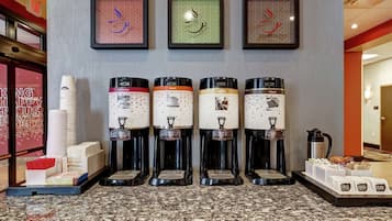 Um espaço de café com quatro dispensadores, uma pilha de copos descartáveis e uma bandeja com cápsulas de café.
