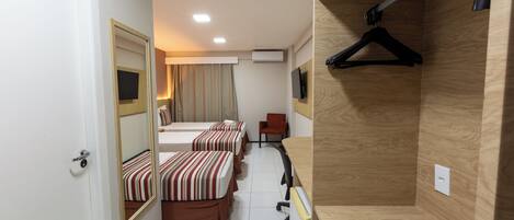 Quarto de hotel com cama, cadeira, escrivaninha e espelho.