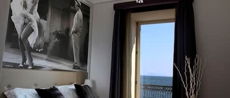 Quarto com uma cama grande, um candelabro, vista para o mar e um quadro na parede.