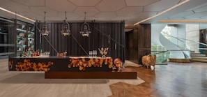 Uma área de bar moderna com um balcão comprido, várias luminárias pendentes e um detalhe decorativo central.