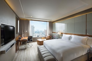 Quarto de hotel com uma cama grande, escrivaninha com televisão de tela plana, uma cadeira e vista para a paisagem urbana.
