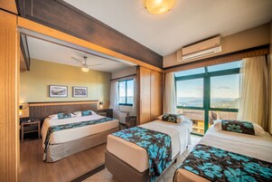 Quarto de hotel com duas camas, um ventilador de teto e uma janela grande com vista para as montanhas.
