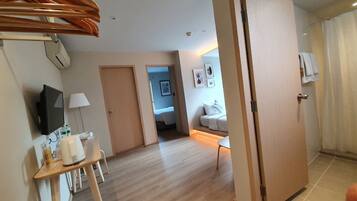 Quarto de hotel com piso de madeira, televisão, escrivaninha com abajur e uma cama ao fundo.