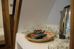 Uma mesa branca com disposição para café da manhã, incluindo um cesto de cápsulas de café, uma cafeteira e vários copos.