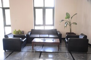 Uma sala de estar moderna com sofá de couro preto, mesa de centro de madeira e um vaso com planta.