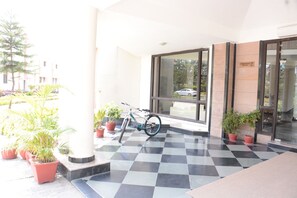 Um chão xadrez, uma bicicleta e vasos de plantas na área de entrada de um edifício.