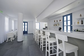 Uma área de bar moderna com banquetas brancas, um balcão longo e prateleiras com garrafas.