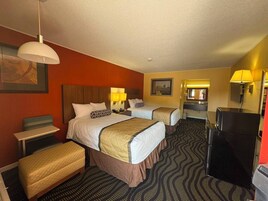 Quarto de hotel com duas camas, uma escrivaninha, uma cadeira, um refrigerador e um espelho.