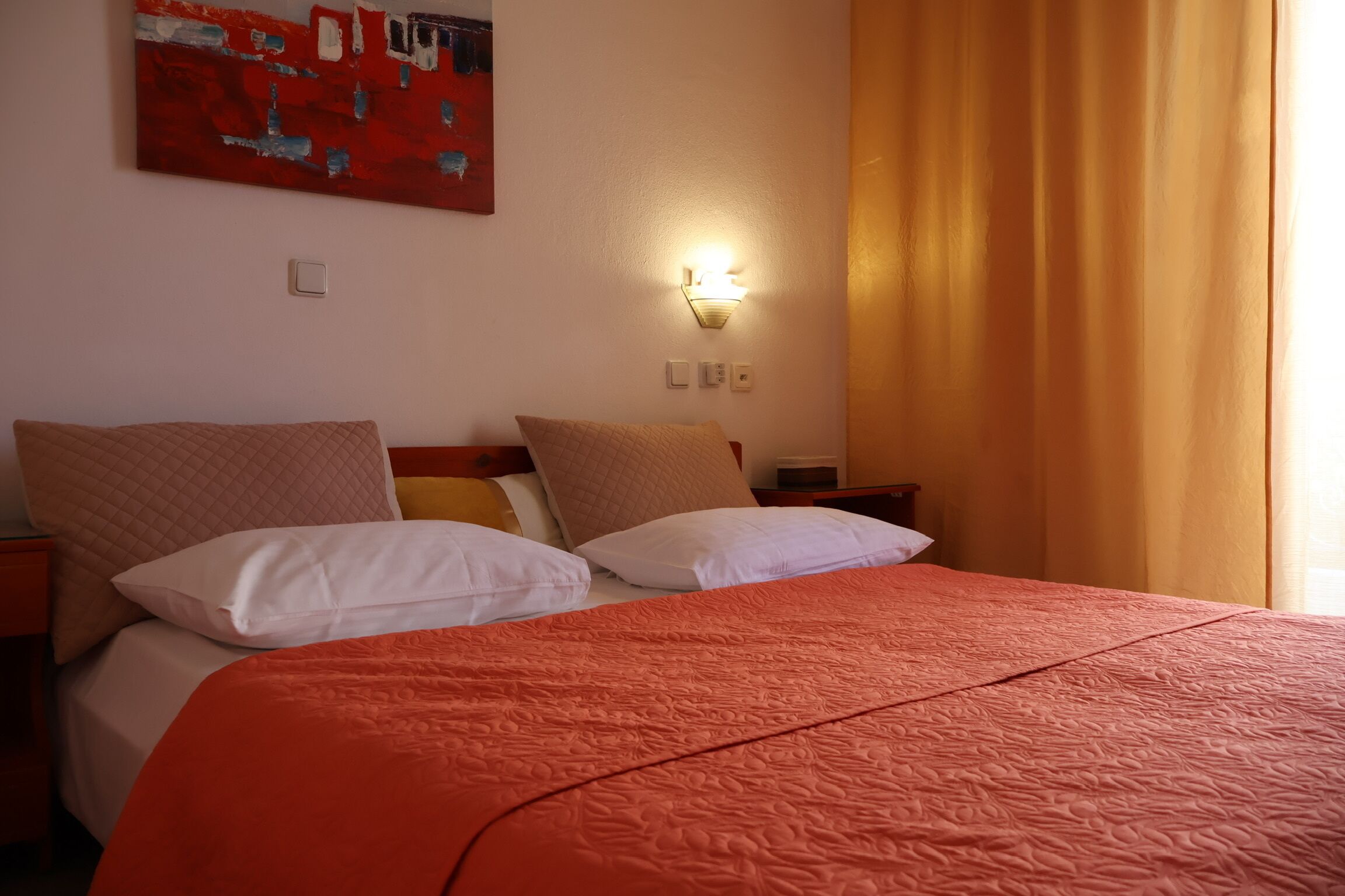 Quarto de hotel com cama, um quadro na parede, mesa de cabeceira e luminária.