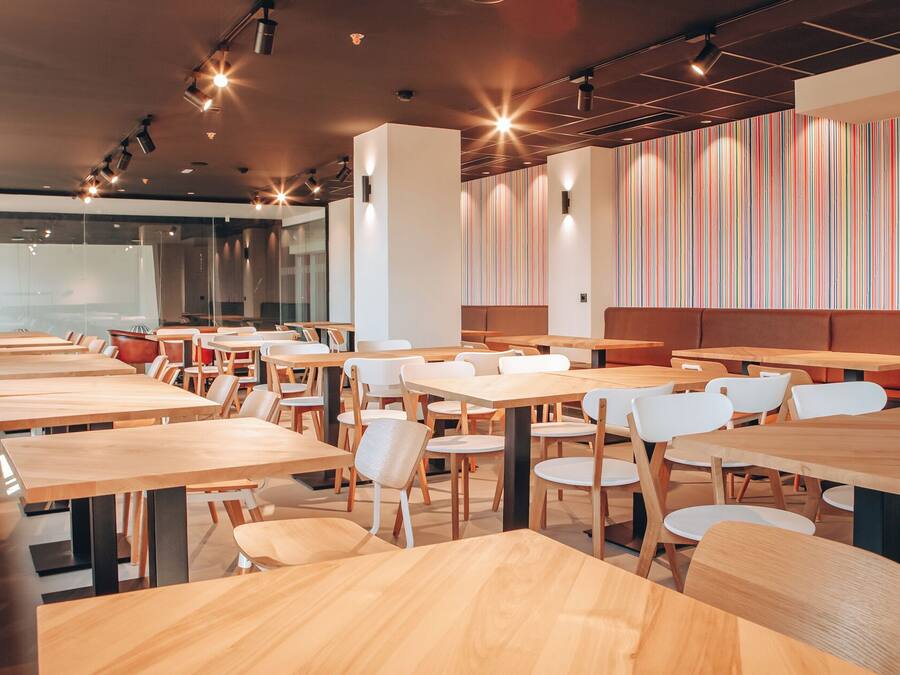 Interior moderno de restaurante com mesas e cadeiras de madeira, decoração na parede com listras e iluminação embutida no teto.
