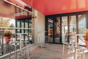 Uma área externa com assentos, banquetas de metal e um toldo vermelho com a inscrição 'FOODSPACE'.