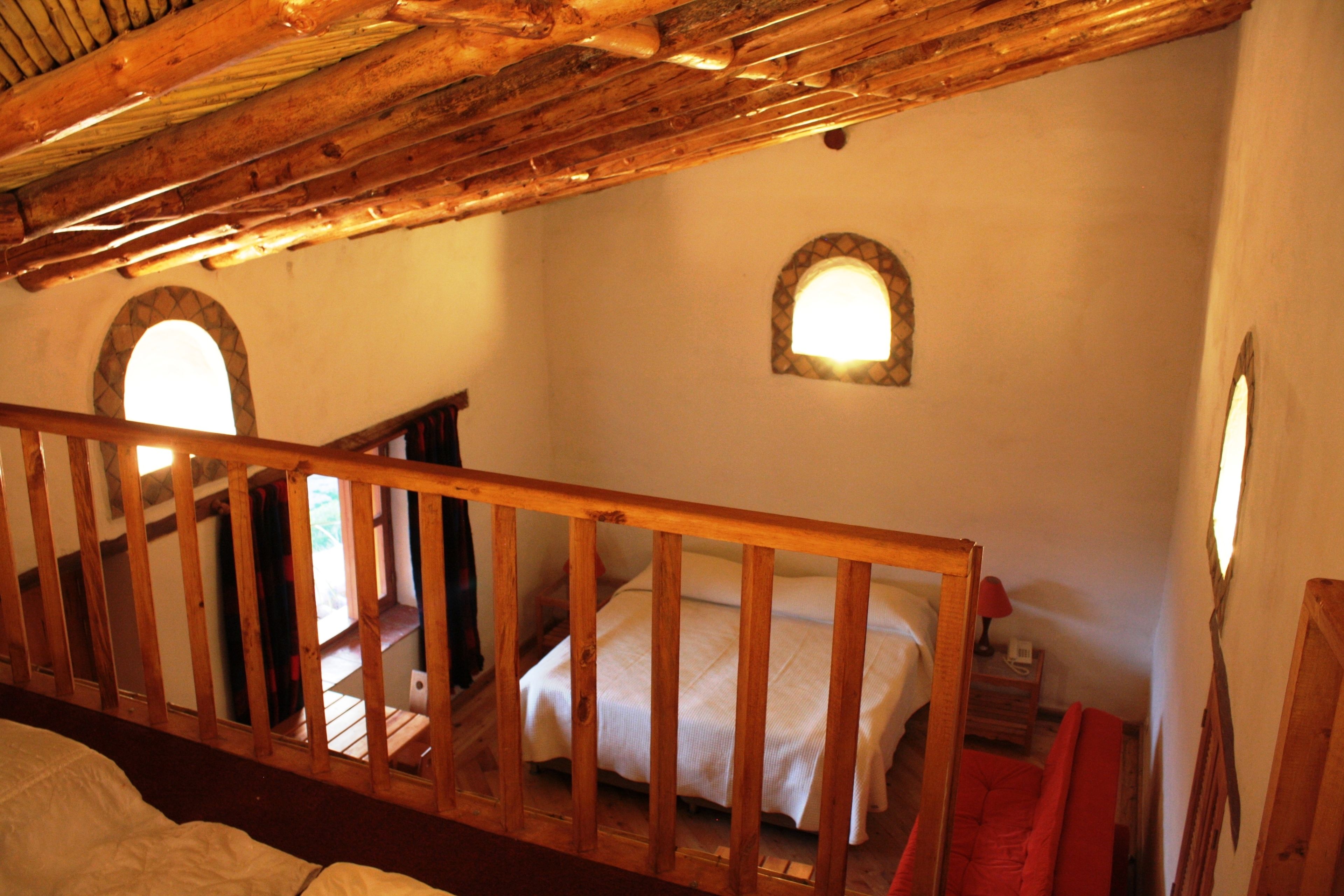Quarto com teto de madeira, cama, mesa de cabeceira e uma pequena janela.