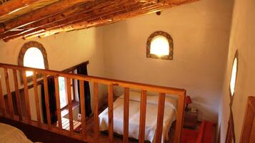 Quarto com teto de madeira, cama, mesa de cabeceira e uma pequena janela.