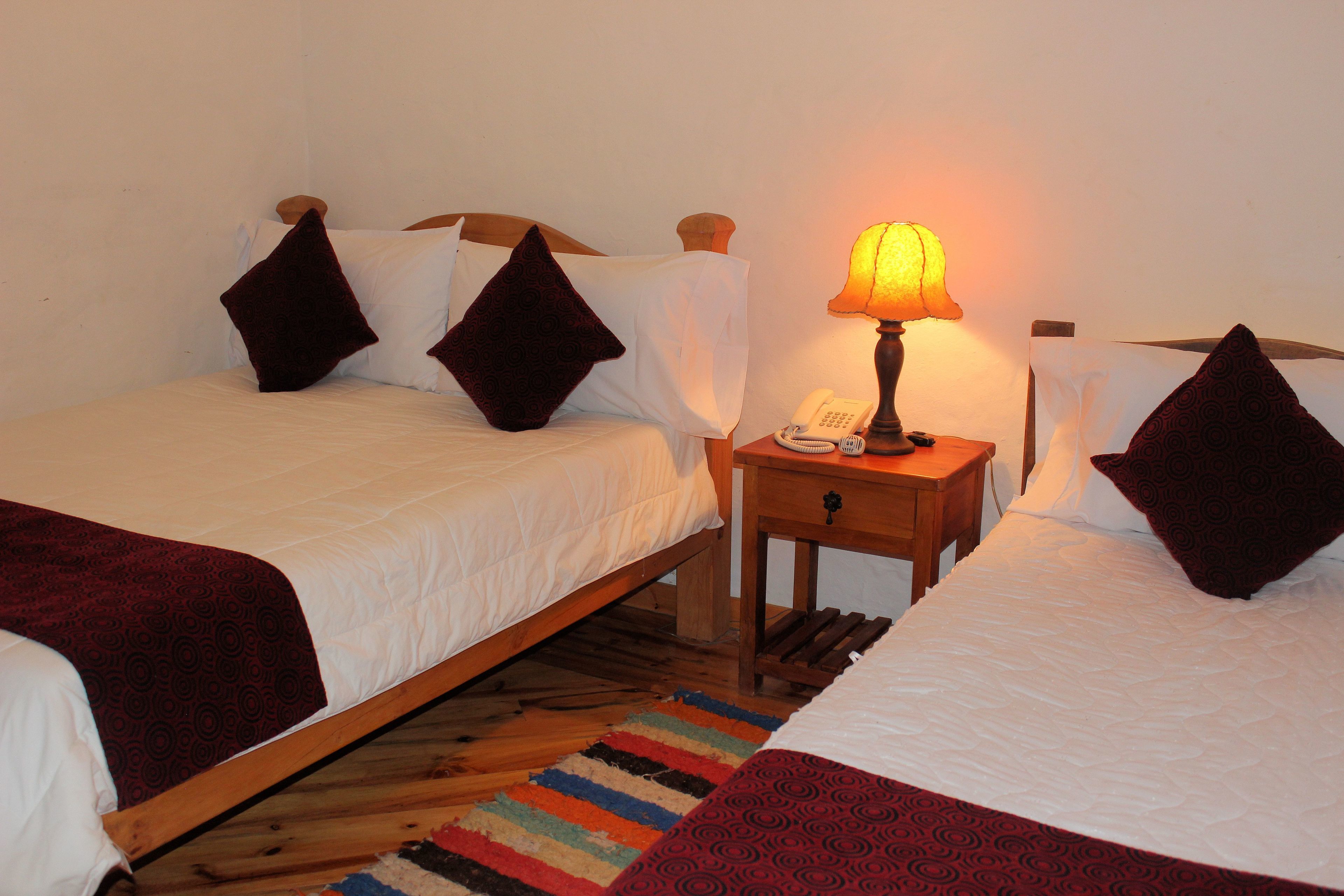 Uma cama de casal com estrutura de madeira, uma mesa de cabeceira com abajur e um tapete listrado.