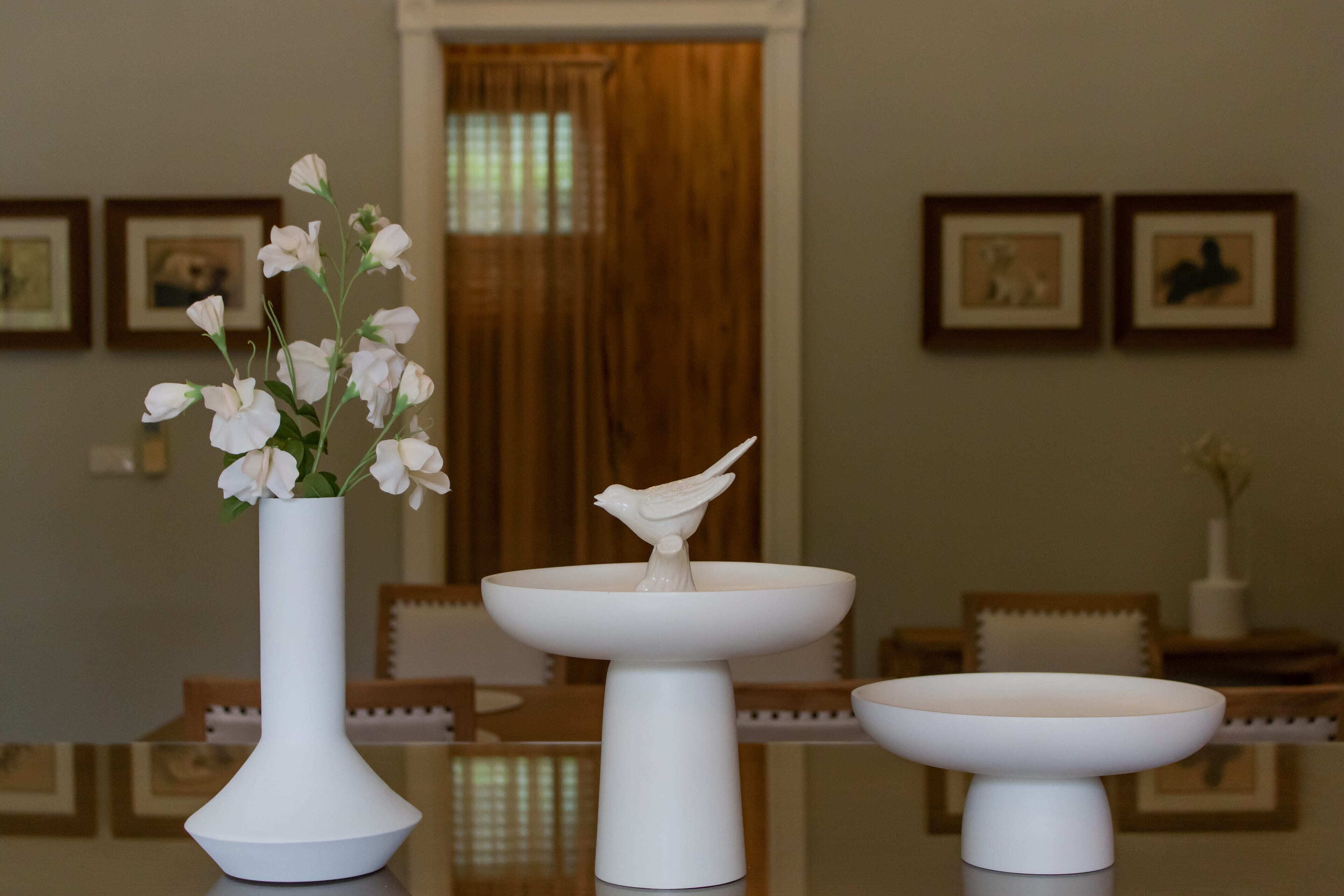 Uma mesa de jantar com um vaso branco e um centro de mesa em forma de pássaro.