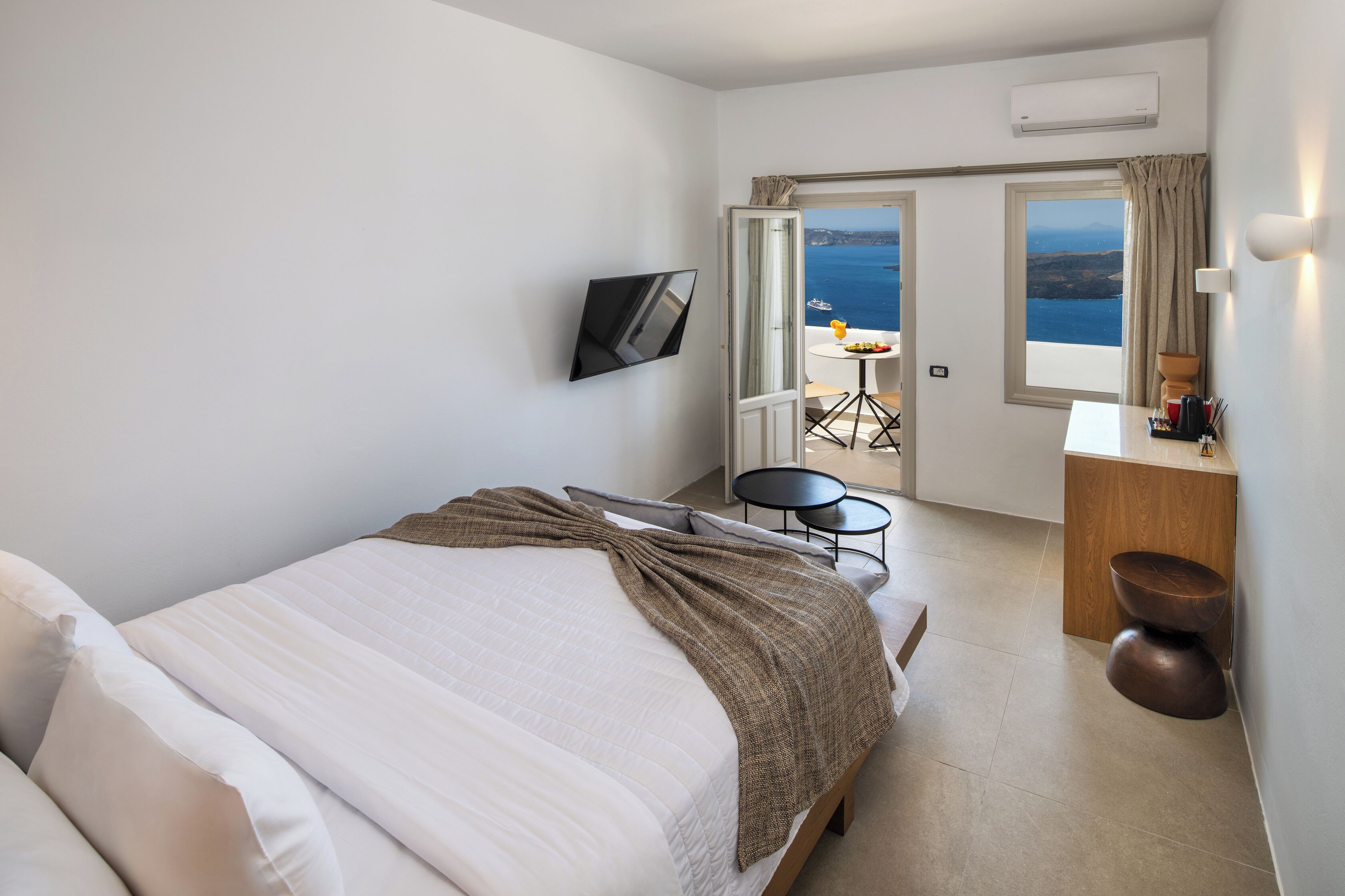 Quarto de hotel com cama, televisão, escrivaninha e uma cadeira, além de vista para o mar.