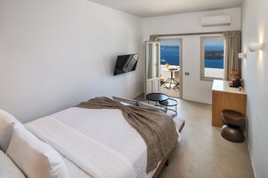 Quarto de hotel com cama, televisão, escrivaninha e uma cadeira, além de vista para o mar.