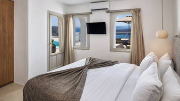 Quarto com uma cama, televisão na parede e vista para o mar pela janela.