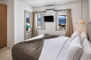 Quarto com uma cama, televisão na parede e vista para o mar pela janela.