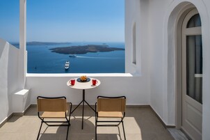 Varanda com mesa e duas cadeiras, vista para o mar com barcos e uma ilha ao longe.