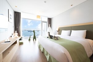 Quarto de hotel moderno com uma cama grande, uma escrivaninha e vista para o mar.