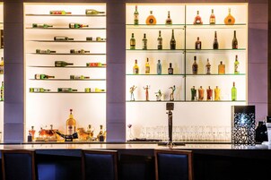 Uma área de bar com prateleiras cheias de garrafas de bebidas, um balcão e assentos.